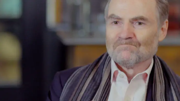 Documentary interviewee in close-up wearing a scarf, speaking on camera.